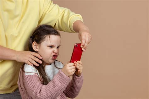 여자의 손 베이지 색 배경에서 멀리 스마트 폰을 복용 부모의 초상화 화가 난 딸은 꽉 전화를 잡고 저항합니다 어린이 의 전화