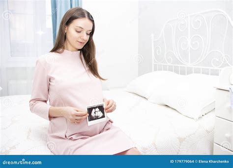 Pregnant Beautiful Girl Is Sitting On The Bed And Her Hands Are On Her