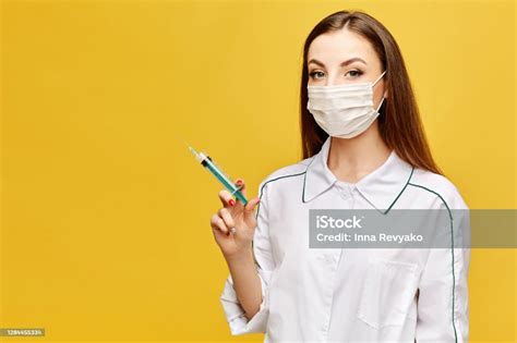 의료복을 입은 젊은 여성의 초상화와 의료 주사기를 손에 들고 보호 마스크를 쓰고 복사 공간이 있는 노란색 배경에서 고립되어