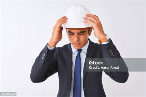 젊은 잘생긴 건축가 남자는 고립 된 흰색 배경 위에 양복과 헬멧을 착용두통 이 절망적으로 고통과 편두통 때문에 스트레스 머리에 손을 걱정하는에 대한 스톡 사진 및 기타