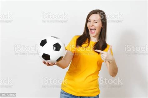 아름 다운 유럽 젊은 쾌활 한 행복 한 여자 축구 팬 또는 플레이어 축구공에 가리키는 노란색 유니폼에 흰색 배경에 고립 스포츠