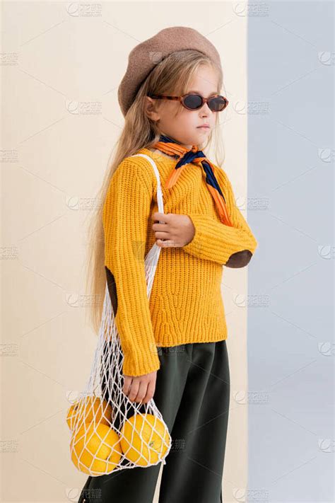 穿着秋装的金发姑娘，戴着太阳镜，头戴米黄色和白色相间的丝带袋，头戴柚子