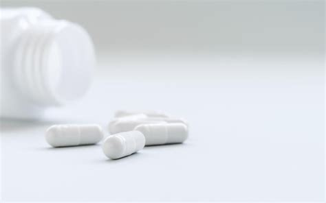 Cápsulas de pastillas blancas vertidas de un frasco blanco tratamiento