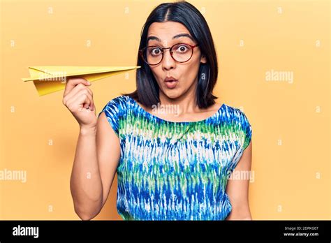Young Beautiful Latin Woman Holding Paper Airplane Scared And Amazed