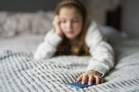 Unhappy Teenage Girl With Mobile Phone Lying On Bed At Home Anxious