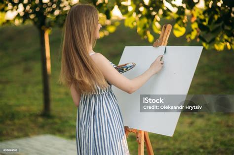 아름 다운 소녀는 팔레트를 사용 하 여 페인트와 주걱 공원에서 그림을 그립니다 이 젤과 캔버스 그림 여름에는 화창한 날 일몰