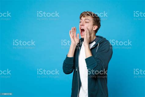 캐주얼 복장에 젊은 남자의 초상화를 옆으로 찾고 스튜디오에서 파란색 배경에 고립 된 입 근처 손 제스처와 비명 사람들은 진심으로