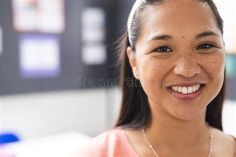 A Young Biracial Female Teacher In Classroom Smiles At Camera With Copy