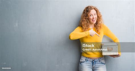 손과 손가락으로 가리키는 매우 행복 상자를 들고 회색 그런 지 벽에 빨강 머리 젊은 여자 가리키기에 대한 스톡 사진 및 기타