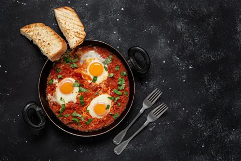 검은 콘크리트 배경에 건배와 팬에 Shakshuka 계란 매운 토마토 페퍼 소스에 데친 달걀 전통적인 유대인 스크램블 계란 상단
