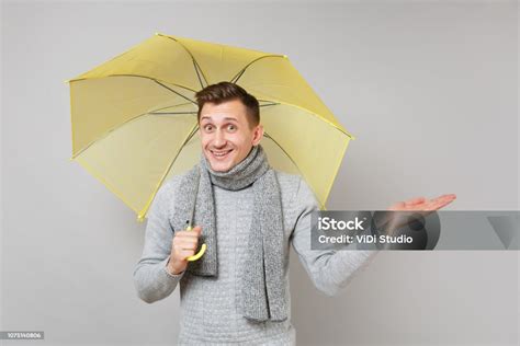 회색 스웨터에서 즐거운 젊은 남자 스카프 잡고 손을 옆으로 회색 바탕에 절연을 가리키는 노란 우산 건강 패션 라이프 스타일