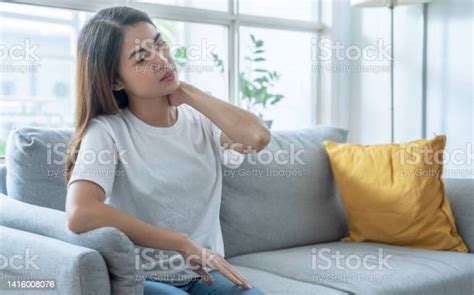 Asian Young Woman Suffering Neck Pain Sitting On Sofa Couch At Home