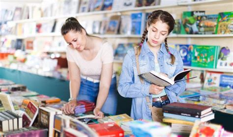 Mujer Feliz Sonriente Mostrando Libro Abierto A La Chica En La Tienda De Libros Foto De Archivo