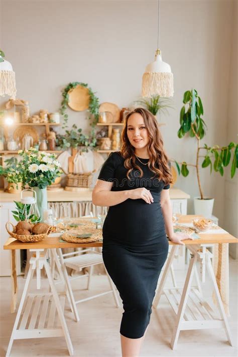 An Attractive Pregnant Woman In A Black Dress In The Kitchen Of The