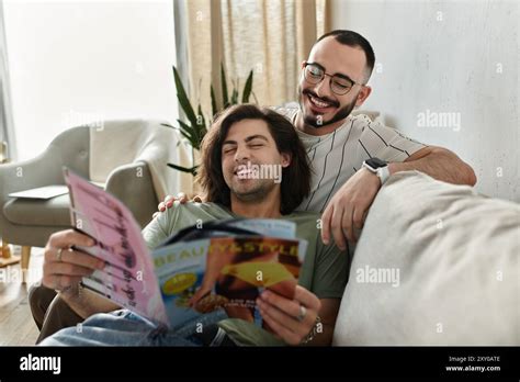 A Gay Couple Relaxes On A Couch Laughing Together While Reading A