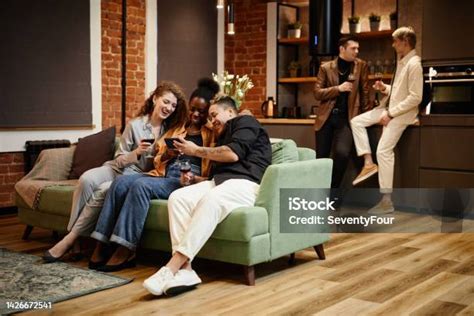 소파에서 스마트 폰으로 사진을 들여다 보는 세 명의 행복한 이문화 소녀 20 24세에 대한 스톡 사진 및 기타 이미지 20