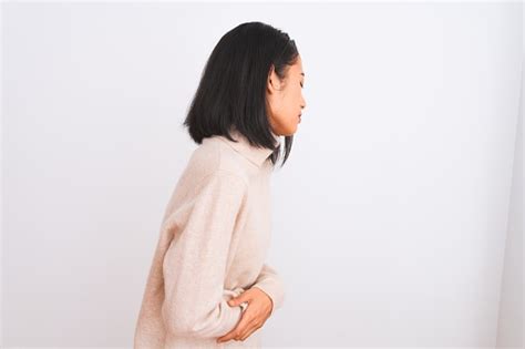 소화 불량 고통스러운 질병이 좋지 않아 위장에 손을 얹고 고립 된 흰색 배경 위에 서있는 터틀넥 스웨터를 입은 젊은 중국 여성