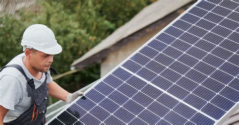 남자 기술자는 집 지붕에 태양광 모듈을 들고 있다 헬멧을 쓴 전기 기사가 야외에 태양 전지판 시스템을 설치하고 있다 대체 및 재생 가능 에너지의 개념입니다 사진