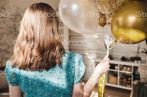 흰색 물방울 무늬가있는 파란색 드레스를 입은 어린 아름다운 소녀는 생일을 축하하고 황금 풍선을 즐깁니다 자기 고립 하는 동안