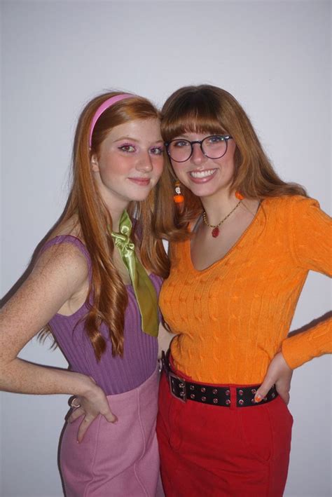 Two Women Standing Next To Each Other In Front Of A White Wall And One