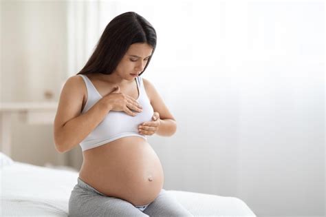 Premium Photo | Pregnant woman sitting on bed massaging her breast