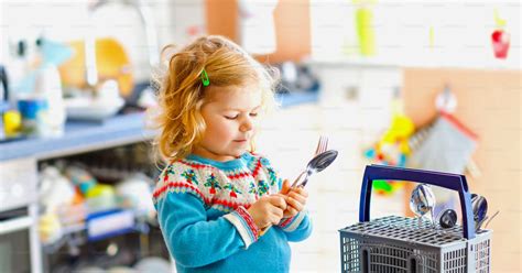 주방에서 식기 세척기를 도와주는 귀여운 어린 소녀 행복하고 건강한 금발의 아이는 나이프 포크 숟가락 칼을 분류합니다 집안일을 돕는 아기 엄마와 아빠 사진