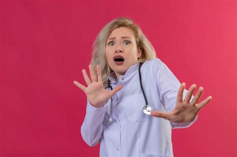 빨간 Backgroung에 아무 제스처를 보여주는 의료 가운에 청진기를 입고 무서 워 젊은 의사 무료 사진