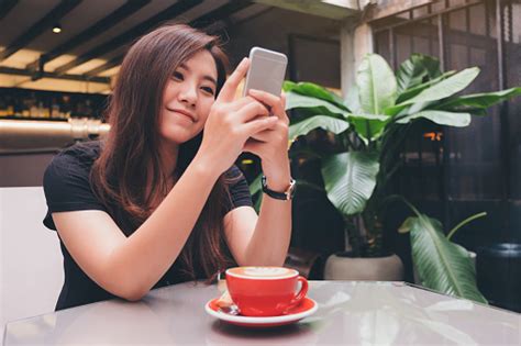 웃는 얼굴 들고와 현대 카페에서 유리 테이블에 빨간 커피 컵 스마트 휴대 전화를 사용 하 여 아름 다운 아시아 여자의 근접 촬영