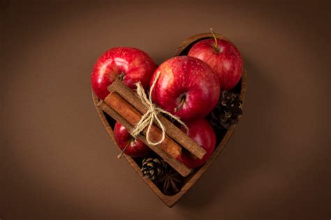 붉은 잘 익은 사과 계피 스틱 갈색 배경에 나무 접시 심장 모양의 소나무 콘 추수 감사절에서 가을 수확 가을 템플릿 사과와 계피