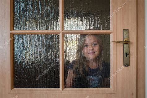 Retrato de una linda niña caucásica escondida detrás de una puerta con ventanas de vidrio