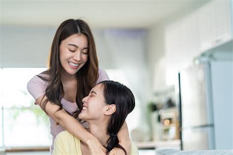 아시아 아름 다운 레즈비언 여자 커플 빗 여자 친구 머리 에 집 매력적인 두 여성 게이 친구는 거실에서 소파에 앉아 함께 미용