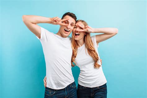 사랑에 젊은 부부 남자와 여자 기쁨과 두 손가락으로 제스처를 보여주는 밝은 파란색 배경에 T 셔츠에 대한 스톡 사진 및 기타 이미지 Istock