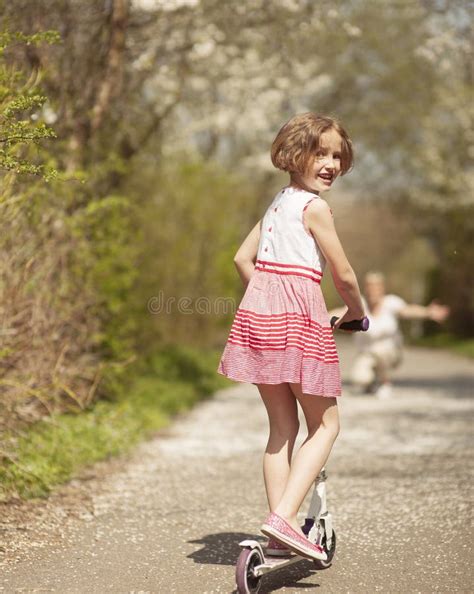 Young Girl Riding Scooter In Park Away From Camera To Mother Stock