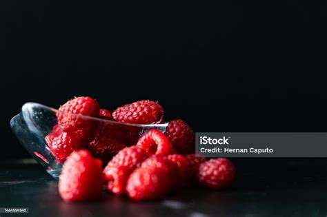 검은 화강암 표면과 검은색 배경에 있는 작고 투명한 그릇에 있는 라즈베리의 서빙의 정상적인 보기 수평 방향 텍스트 공간 0명에