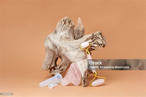현대적인 럭셔리 세련된 뷰티 컨셉 페이셜 마사지 키트와 베이지 색 종이 배경의 나무 뿌리 내추럴 핑크 스톤 웰빙 페이스