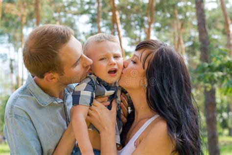 Мама и папа обнимают и целуют их младенца и его ` S капризное Стоковое Фото изображение