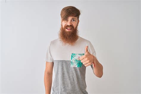 젊은 빨간 머리 아일랜드 남자 T 셔츠를 입고 고립 된 흰색 배경 위에 서 행복 한 엄지 손가락 을 하 고 손으로 제스처 성공을 보여주는 카메라를 보고 표정을 승인합니다 T