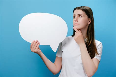 빈 연설 거품을 들고 팔을 퍼뜨리는 것은 파란색 스튜디오 배경 벽에 고립 된 흰색 티셔츠를 입고 턱에 손을 얹고 팔을 벌리는