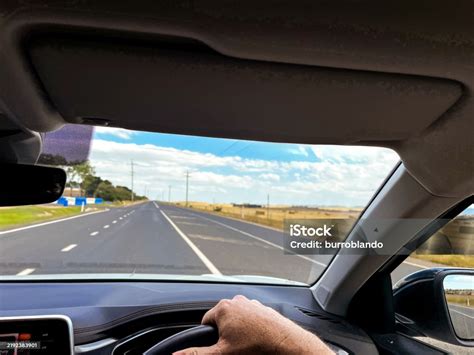 자동차 윈드스크린을 통해 광각으로 보면 솜털이 보송보송한 구름이 낀 맑고 푸른 하늘 아래 실내와 핸들 운전석의 손이 둘러싸인 사막 평원을 가로지르는 고속도로가 드러납니다