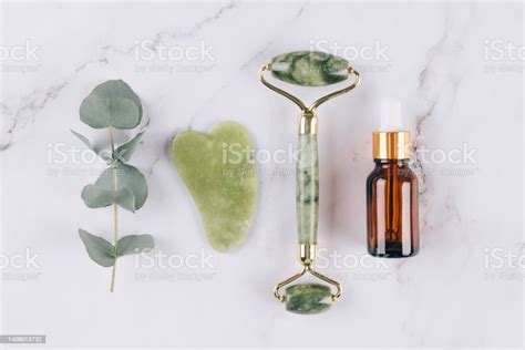 옥 얼굴 롤러와 Gua Sha 스크레이퍼 흰색 대리석 테이블 위에 얼굴 세럼 또는 유기 화장품 오일 리프팅 치료를위한 얼굴