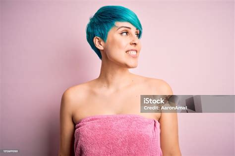 분홍색 배경에 샤워 후 수건을 입고 파란색 패션 머리를 가진 젊은 여성은 얼굴에 미소와 함께 옆으로 찾고 자연스러운 표정 자신감