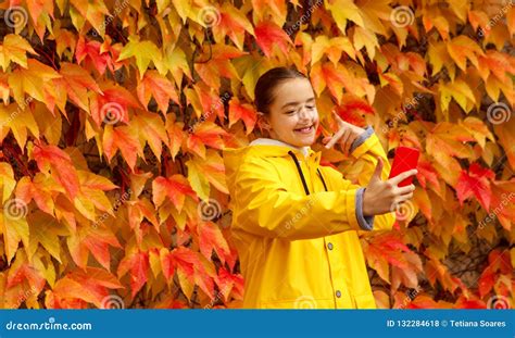 Красивая маленькая девочка в желтом плаще принимает Selfie на яркую ...