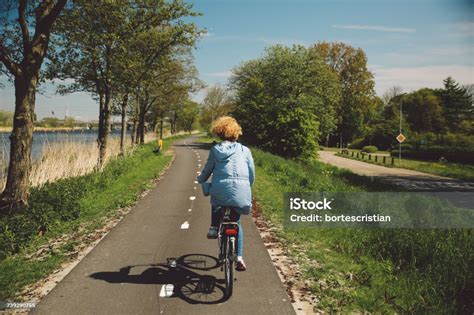 Rear View Of Woman With Curly Hair Riding Bicycle On Road During Sunny