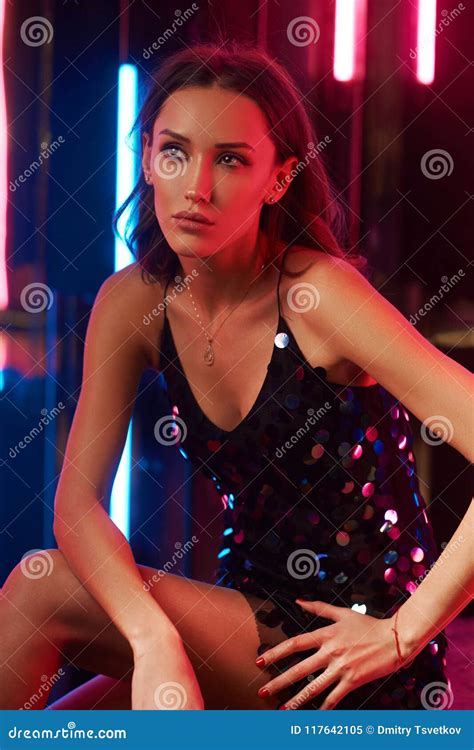Female Model In Black Shiny Cami Dress Sitting On Large Cube And Stock