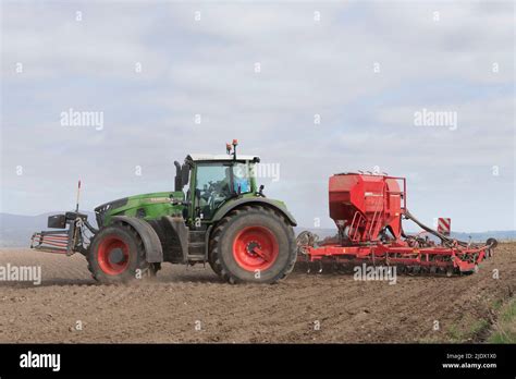 A Fendt Tractor Pulling A Red Seed Drill Turning At The End Of The Field In Which It Is Sowing