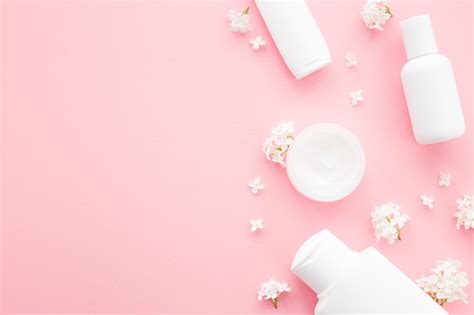 밝은 분홍색 테이블에 꽃잎과 다른 흰색 세 면 도구와 라일락 가지 얼굴 손 다리 및 신체 피부에 대 한 관심 여성 미용 제품