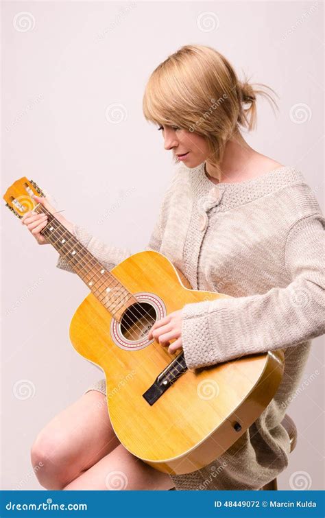 Young Blonde Lady In Gray Sweater Sitting On Chair And Playing Acoustic