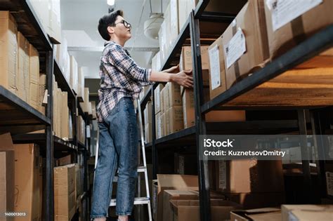 피곤한 여성 창고 노동자가 사다리에 서서 선반에 상자를 놓습니다 사다리에 대한 스톡 사진 및 기타 이미지 사다리 소매 소비자주의 25 29세 Istock