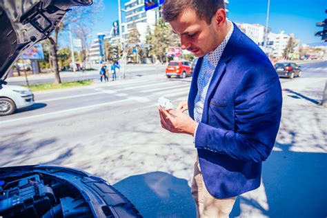 한 사업가가 화창한 바쁜 날에 자동차 기름을 확인하는 동안 대로 옆에 차를 주차했습니다 20 24세에 대한 스톡 사진 및 기타 이미지 20 24세 가까운 갈색