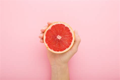 젊은 성인 여성 손 빨간 자몽의 절반을 들고 신선한 과일 라이트 핑크 테이블 배경 파스텔 색상 근접 촬영 하향 보기 감귤류